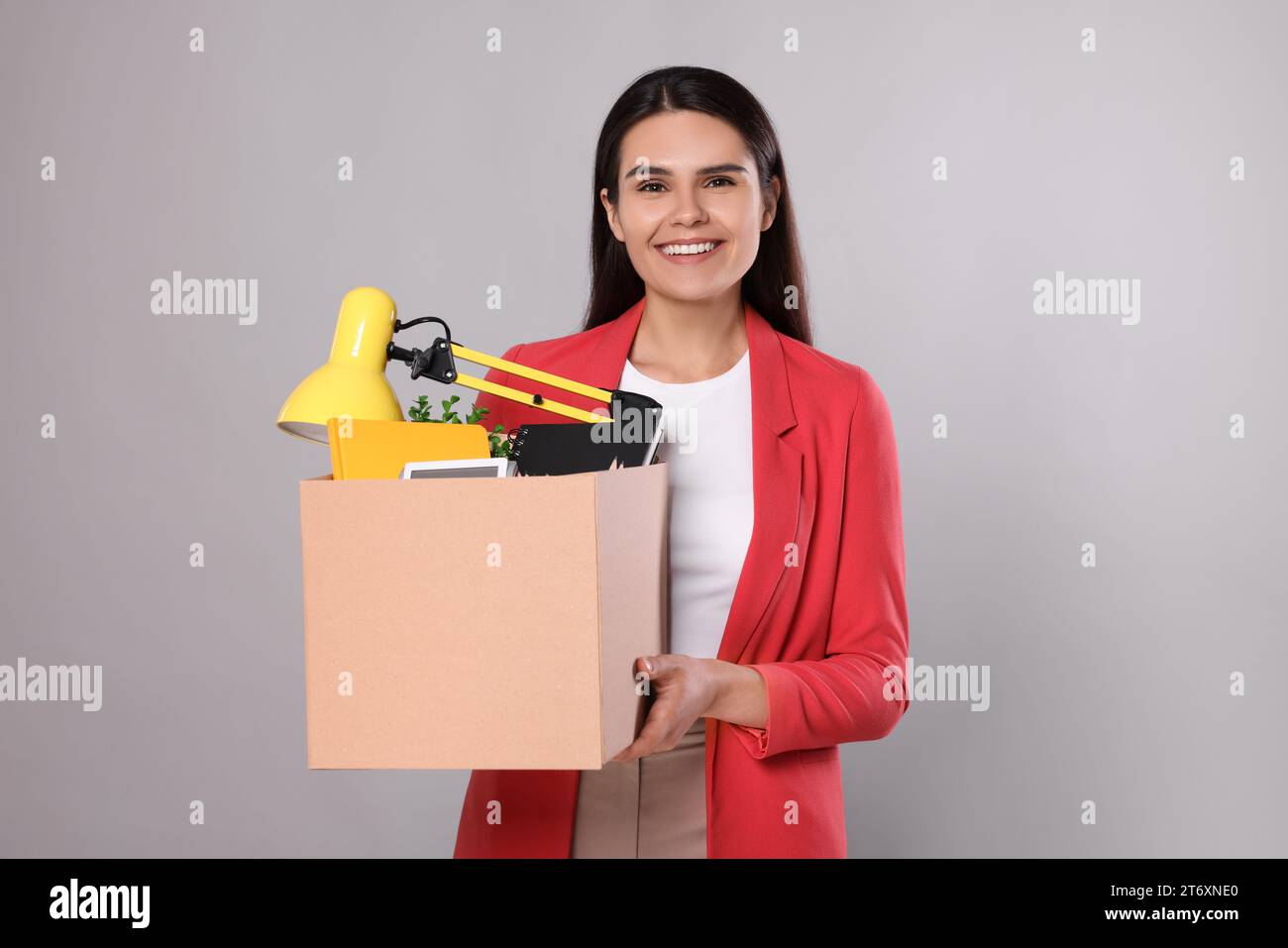 Happy unemployed woman with box of personal office belongings on grey ...