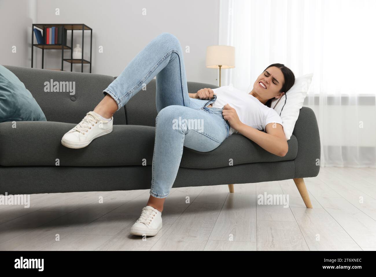 Young Woman Struggling To Squeeze Into Tight Jeans While Lying On Sofa