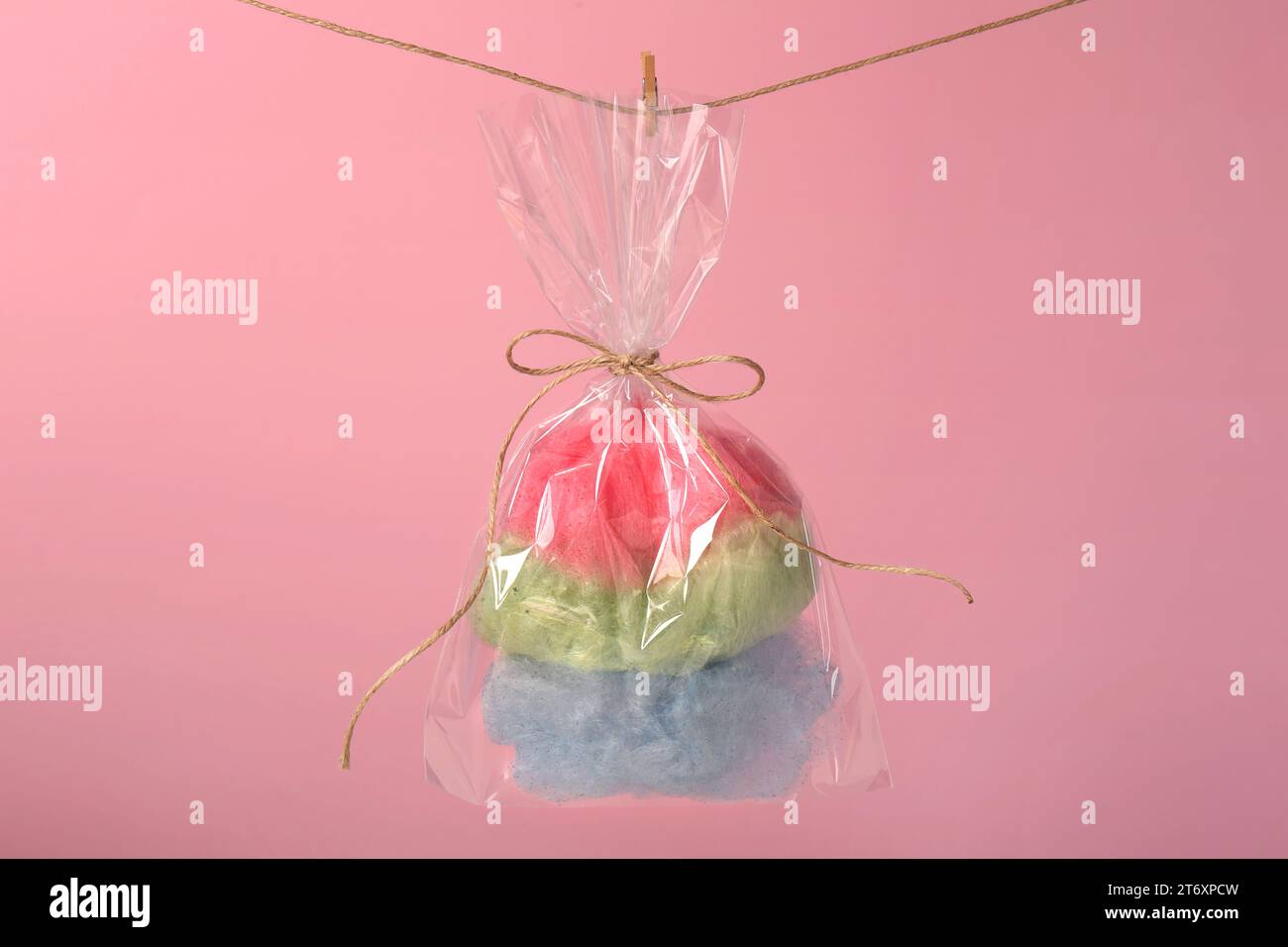 Packaged sweet cotton candy hanging on clothesline against pink ...