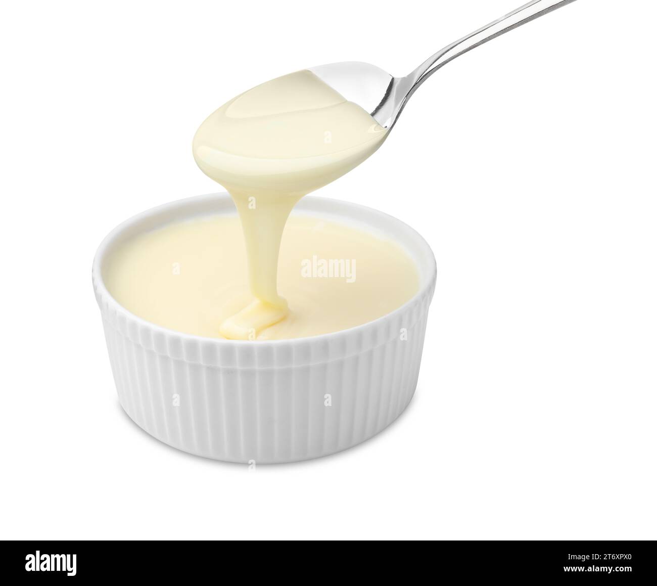 Condensed milk flowing down from spoon into bowl isolated on white ...