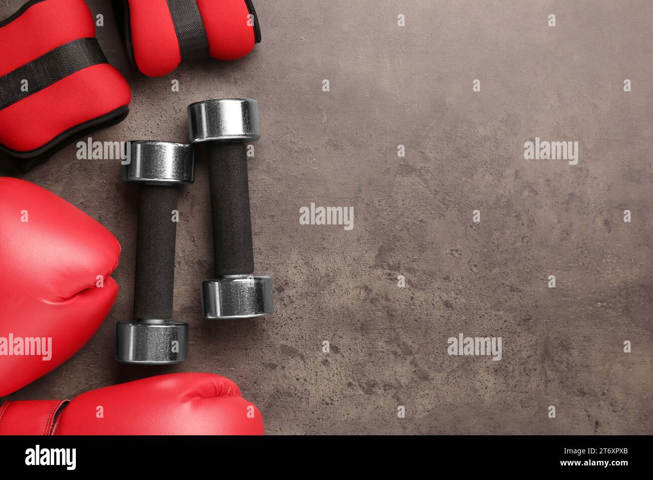 Metal dumbbells, boxing gloves and weights on brown textured table, flat lay. Space for text ...
