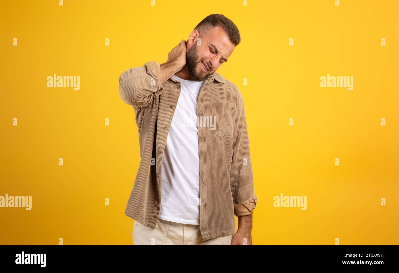 Unhappy millennial european man with beard in casual massaging neck ...