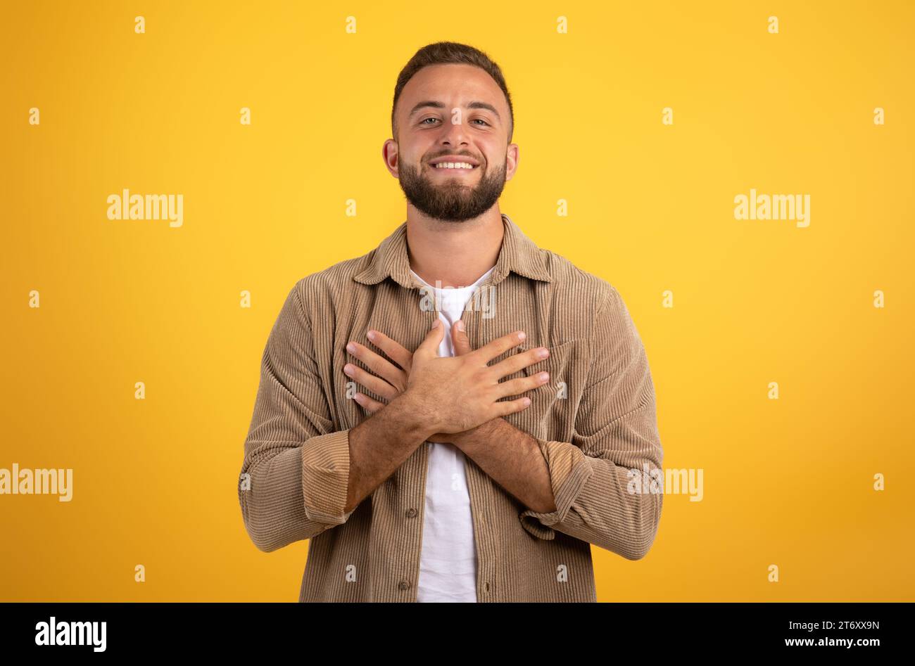 Glad handsome young european man presses hands to chest, isolated on ...