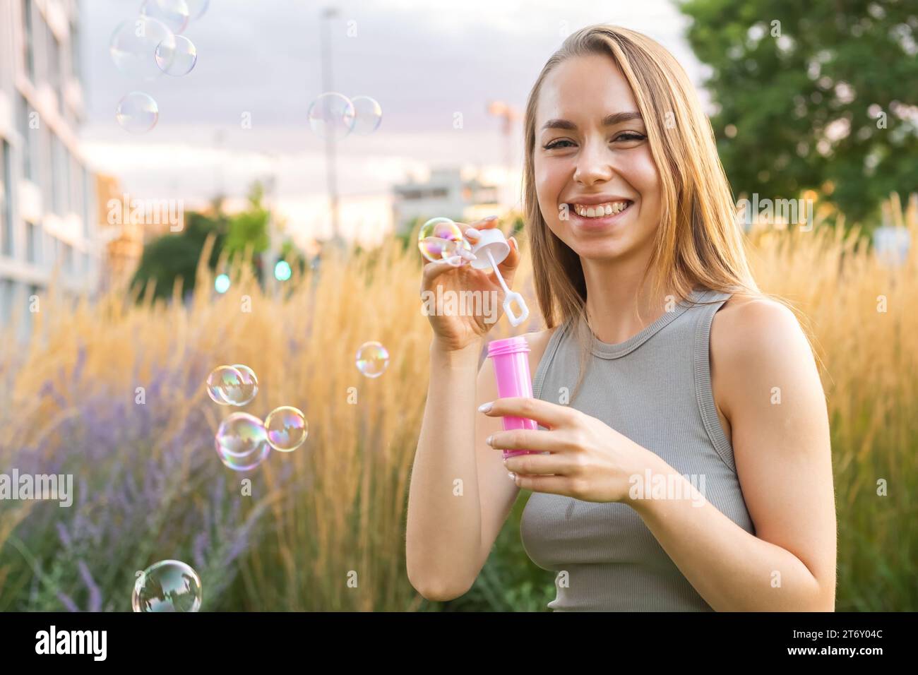 A joyous lady with long, flowing hair creates soap bubbles and smiles ...
