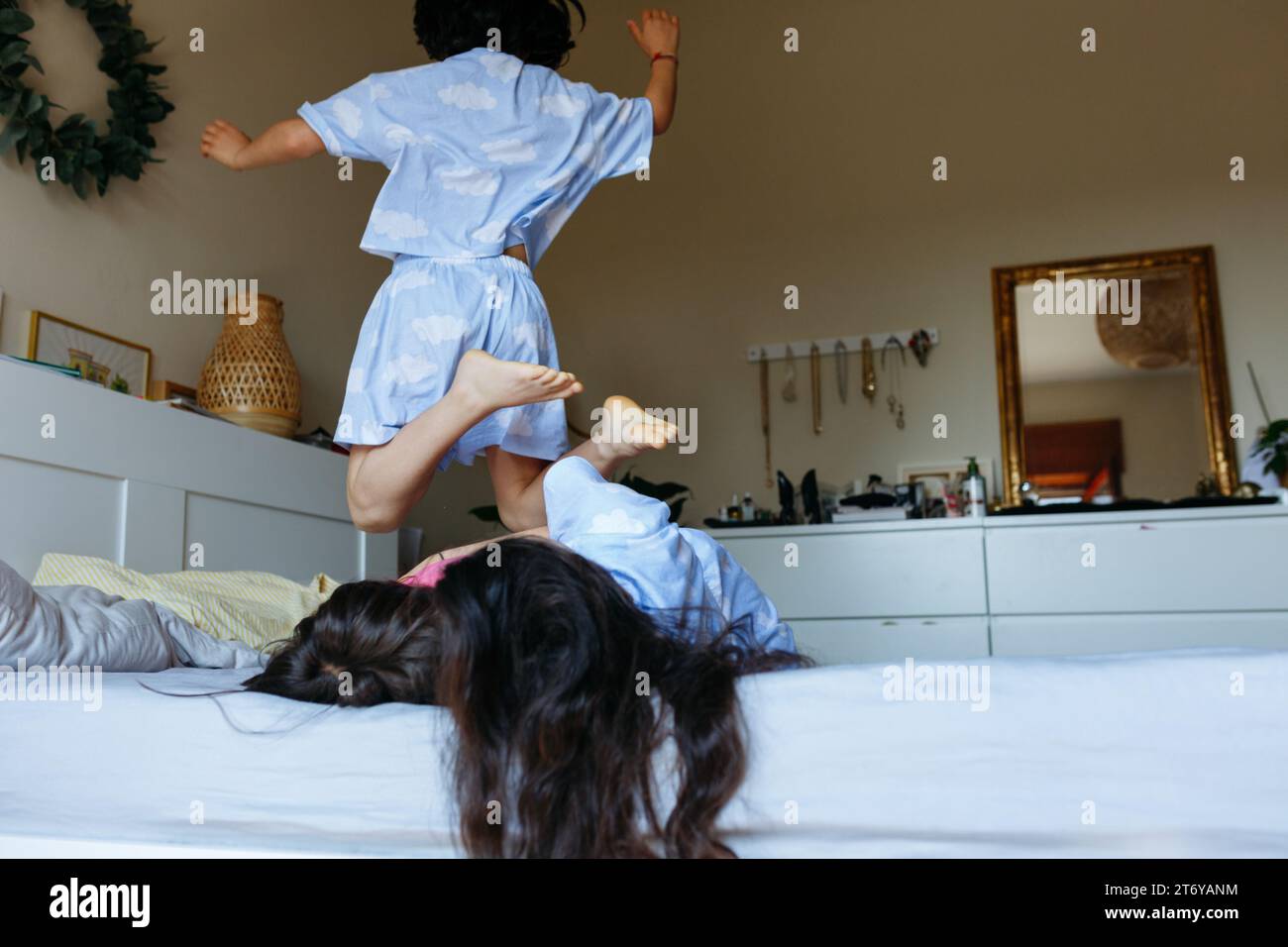 two children lying on the bed and other child in blue pyjamas jumping ...