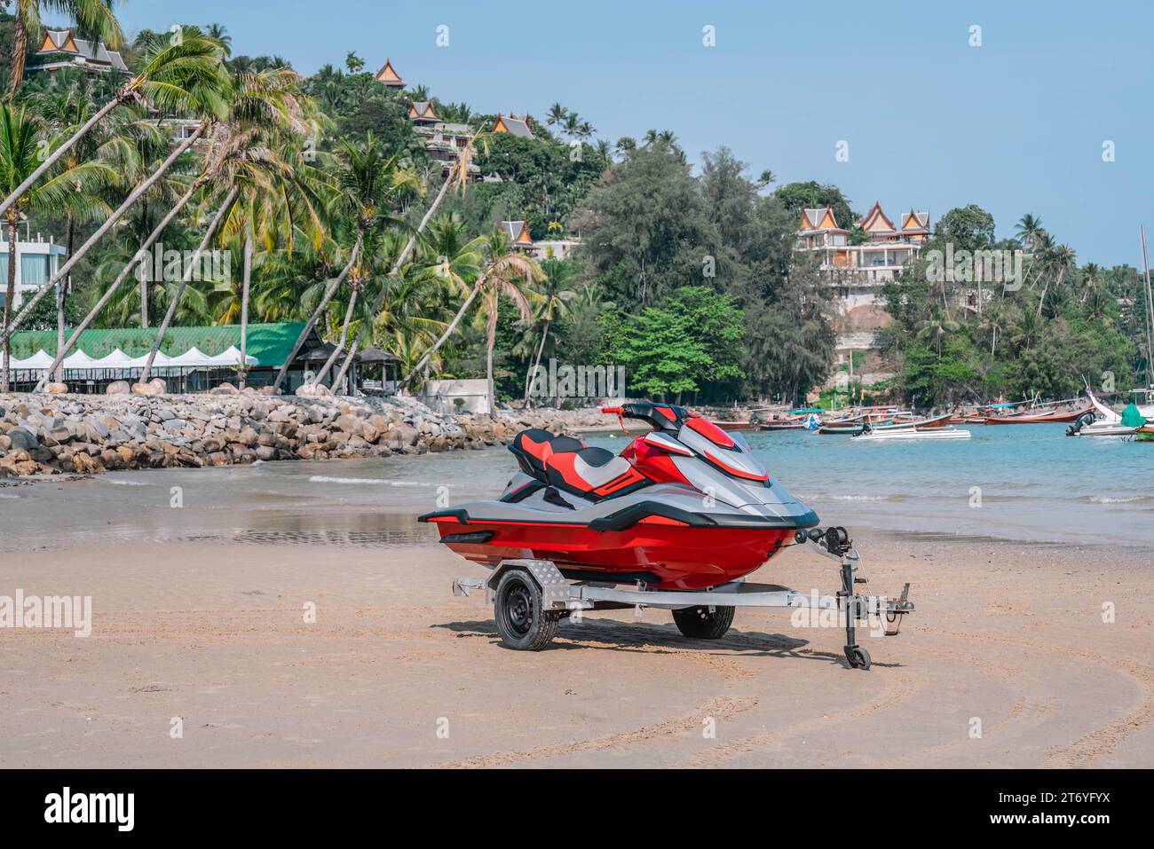 Red jet ski on trailer stands on sand beach, seashore and palm trees ...