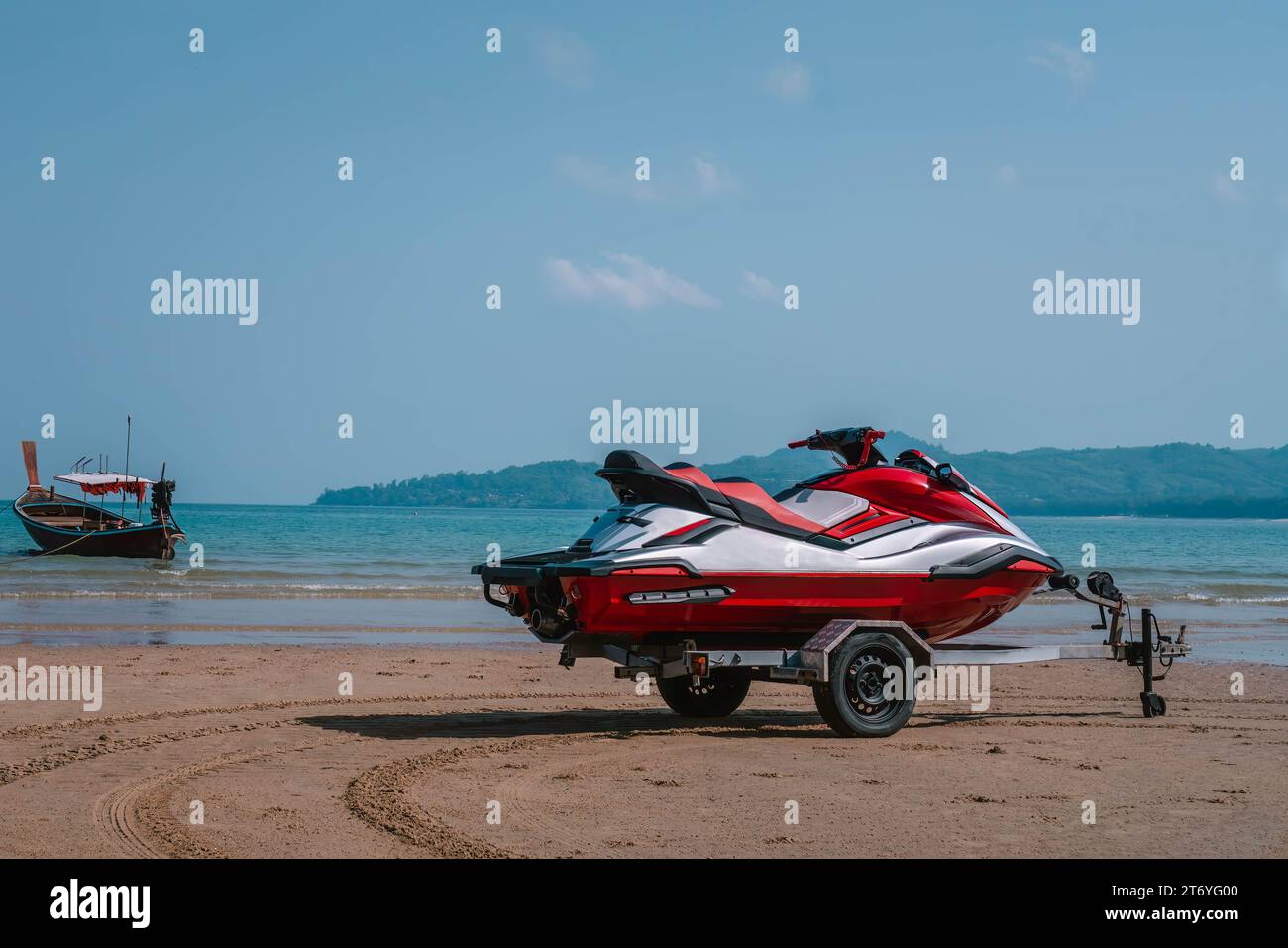 Red jet ski on trailer stands on sand beach, seashore and palm trees ...