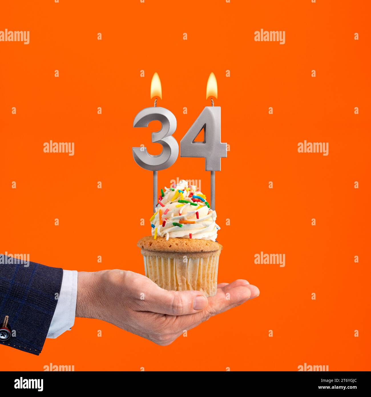 Hand holding birthday cupcake with number 34 candle - background orange ...