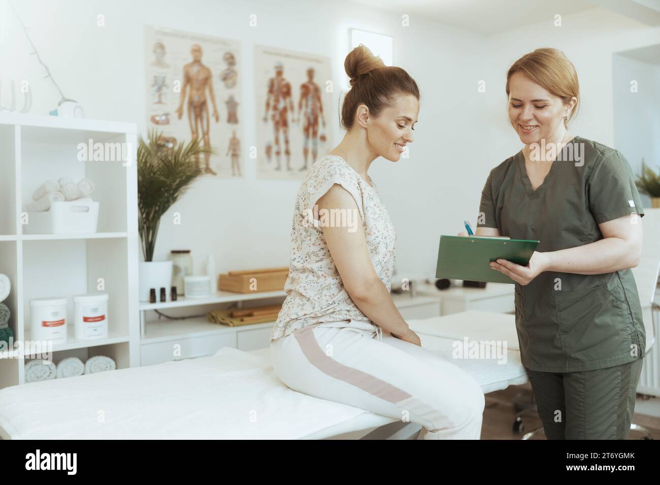 Healthcare time. smiling massage therapist woman in massage cabinet with client doing checkup ...