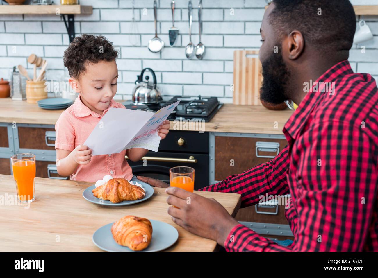Black son reading greeting card while having breakfast with father ...