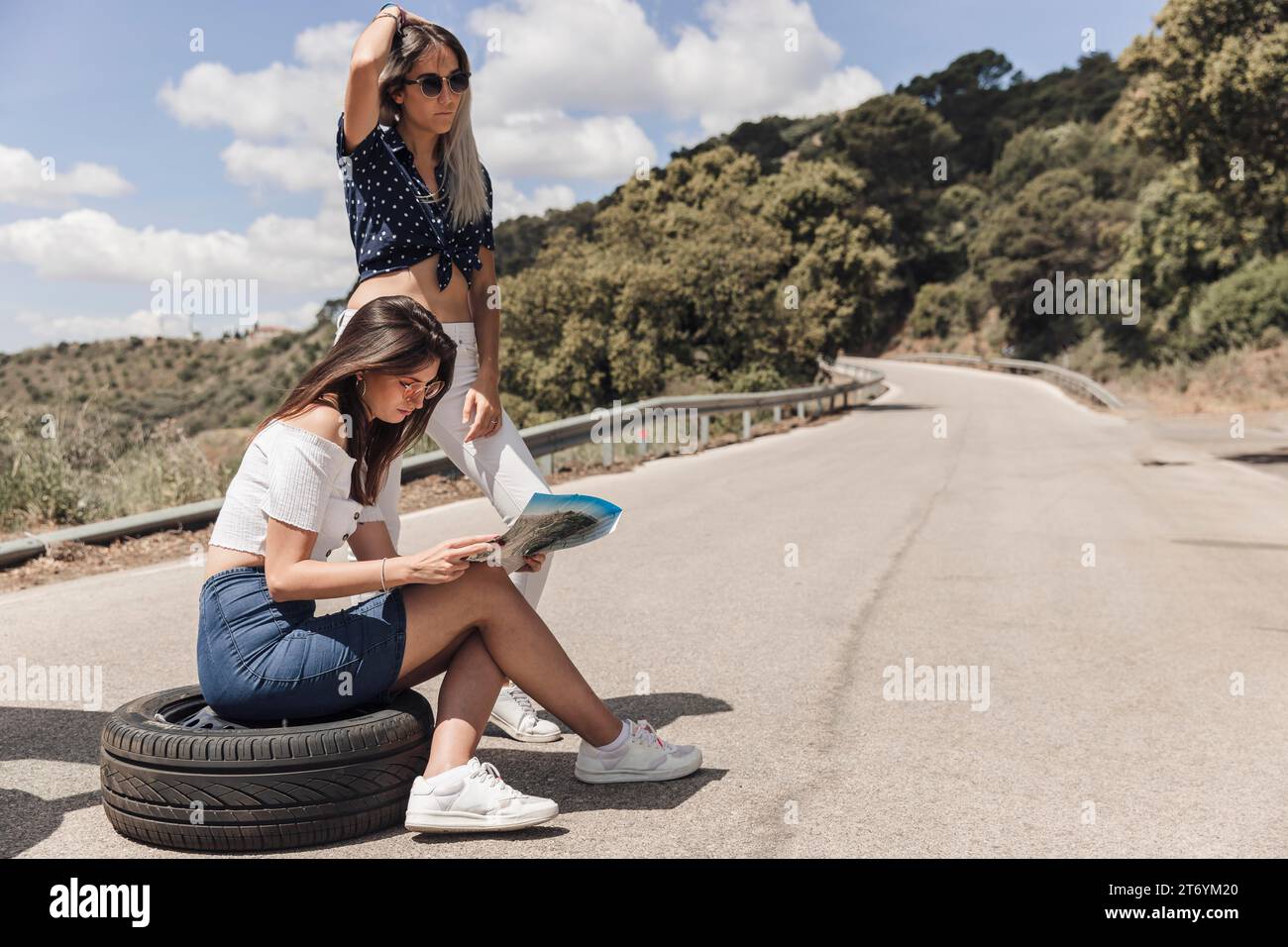 Lost woman sitting tire with her friend looking map Stock Photo - Alamy