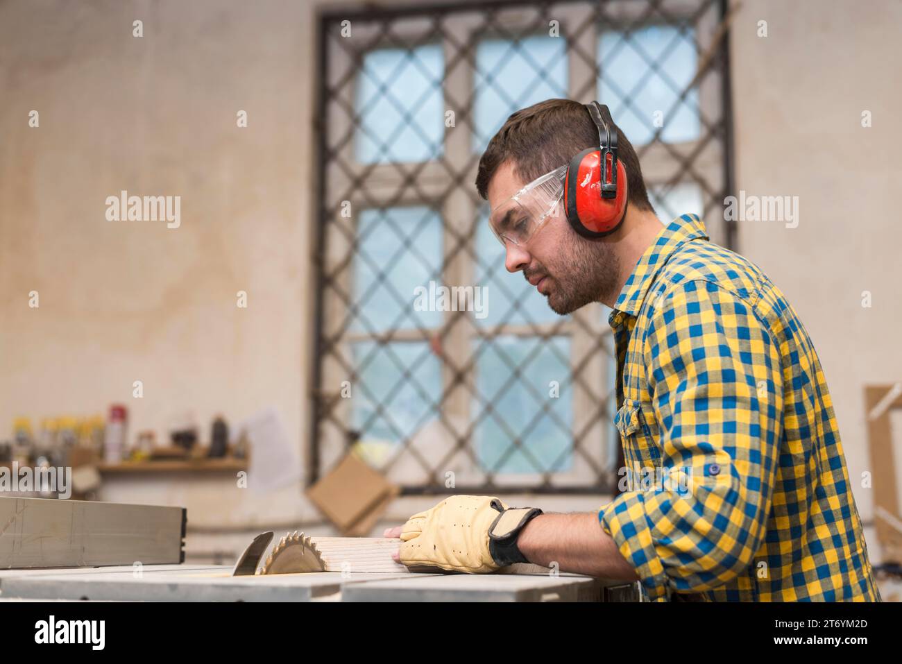 Male carpenter wearing safety glasses ear defender cutting block ...