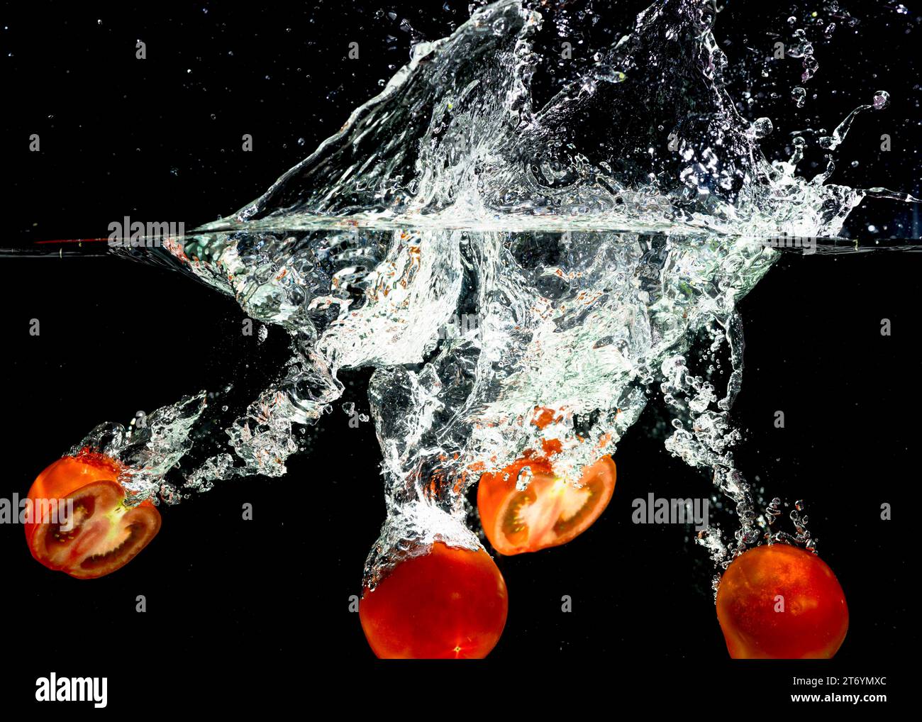 Slices tomatoes falling into splash water against black background ...