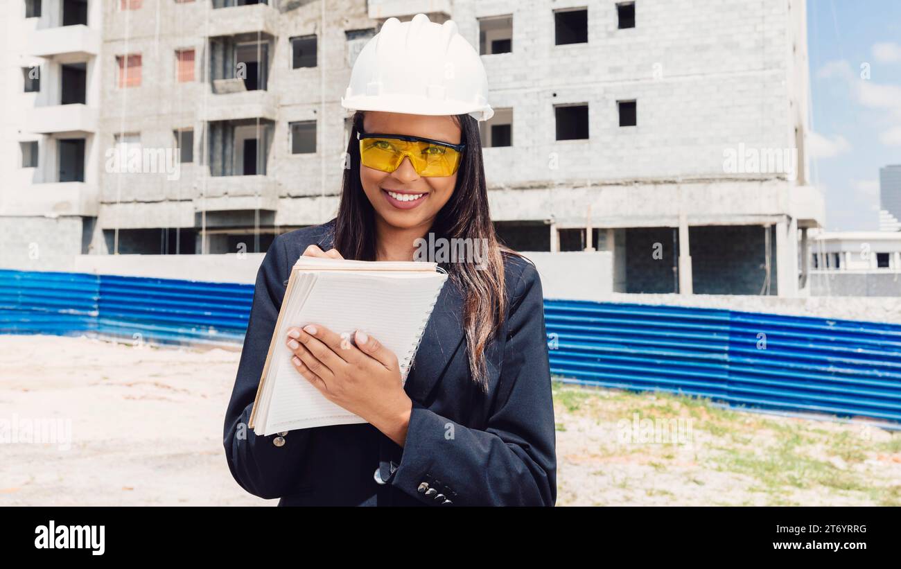 Happy african american lady safety helmet writing notebook near ...