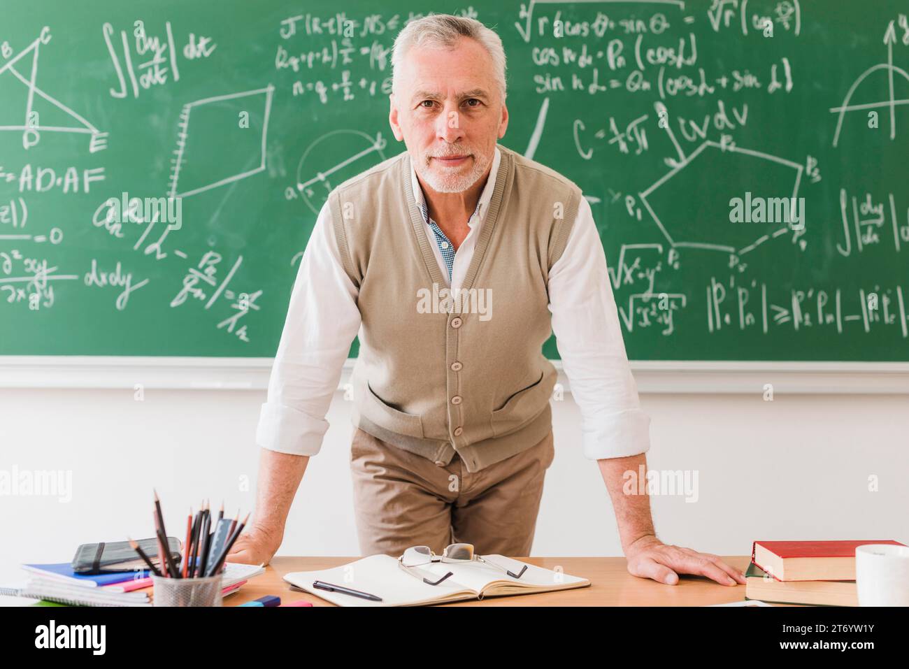 Positive aged math teacher leaning desk Stock Photo - Alamy
