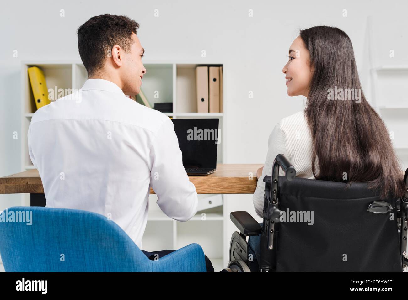 Rear view smiling young business people looking each other workplace ...