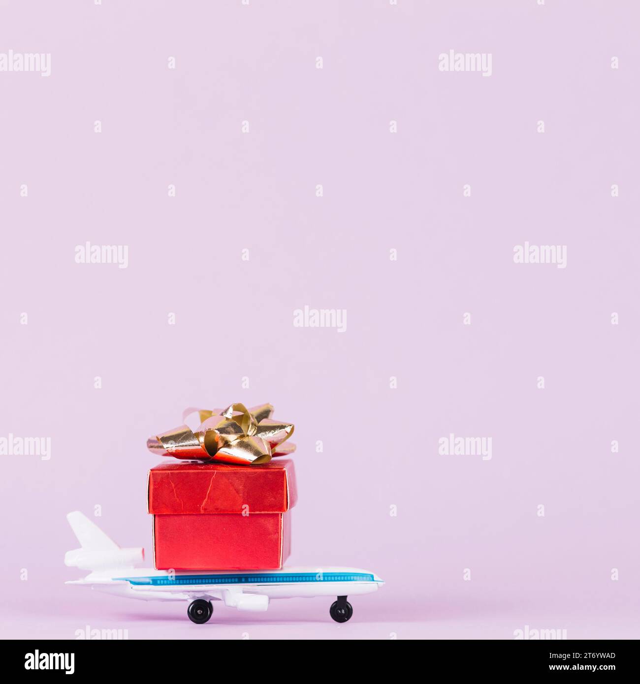 Red giftbox with golden bow toy airplane against pink background Stock ...