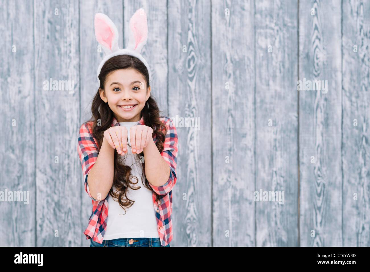 Smiling girl with bunny ears posing like rabbit against gray wooden ...