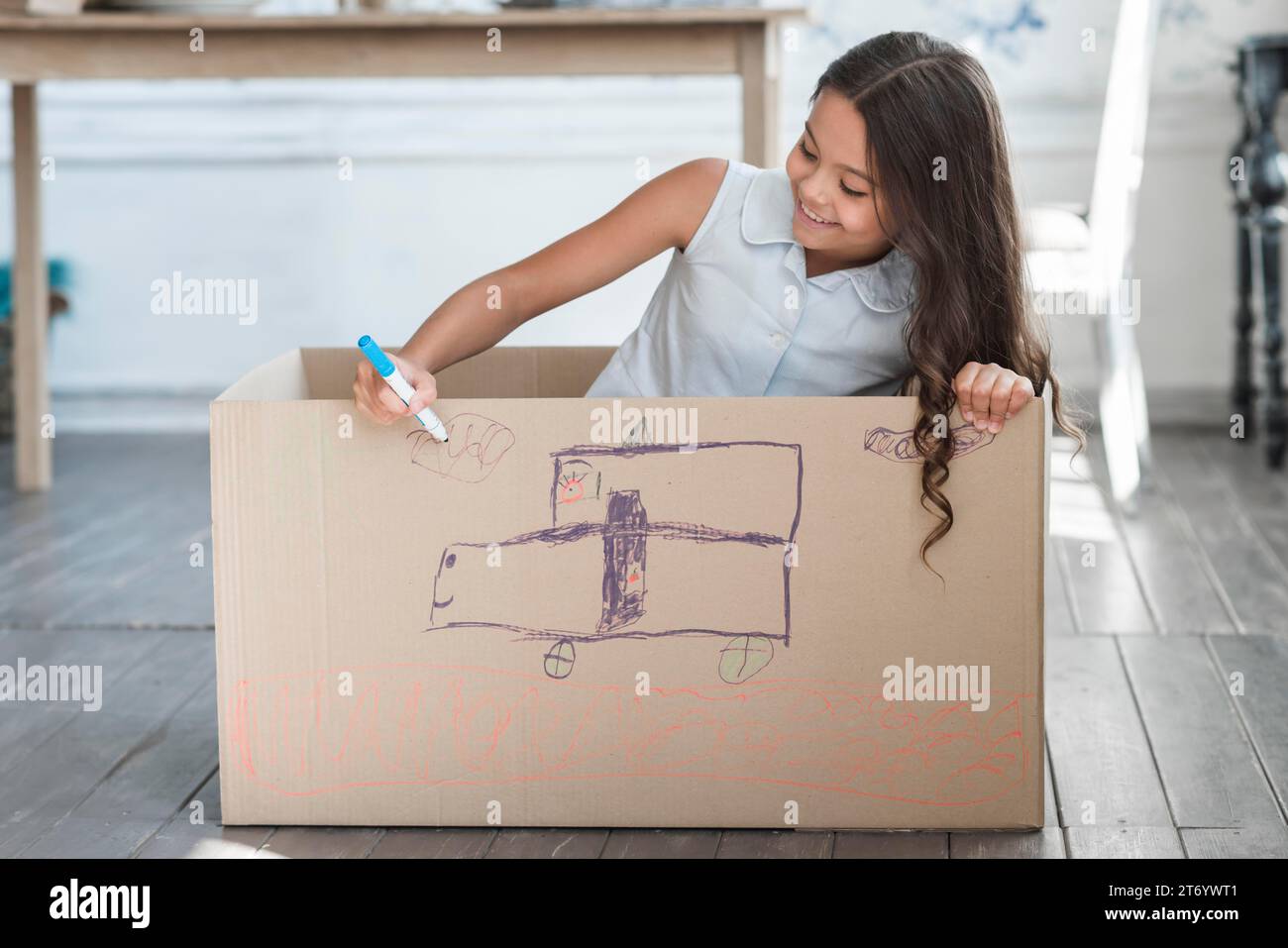 Smiling girl sitting inside cardboard box drawing with marker Stock ...