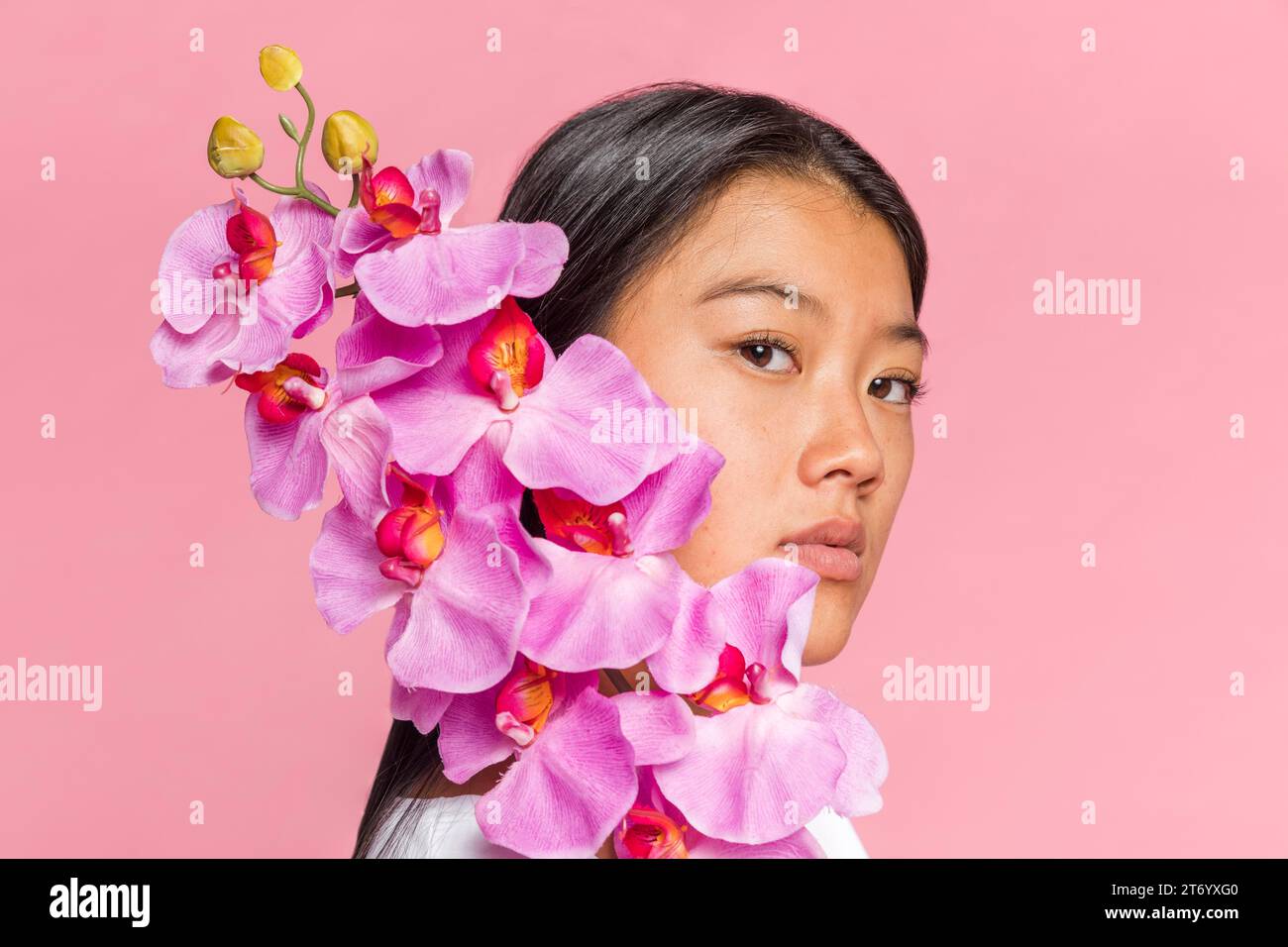 Woman covering her face with orchid looking camera Stock Photo - Alamy