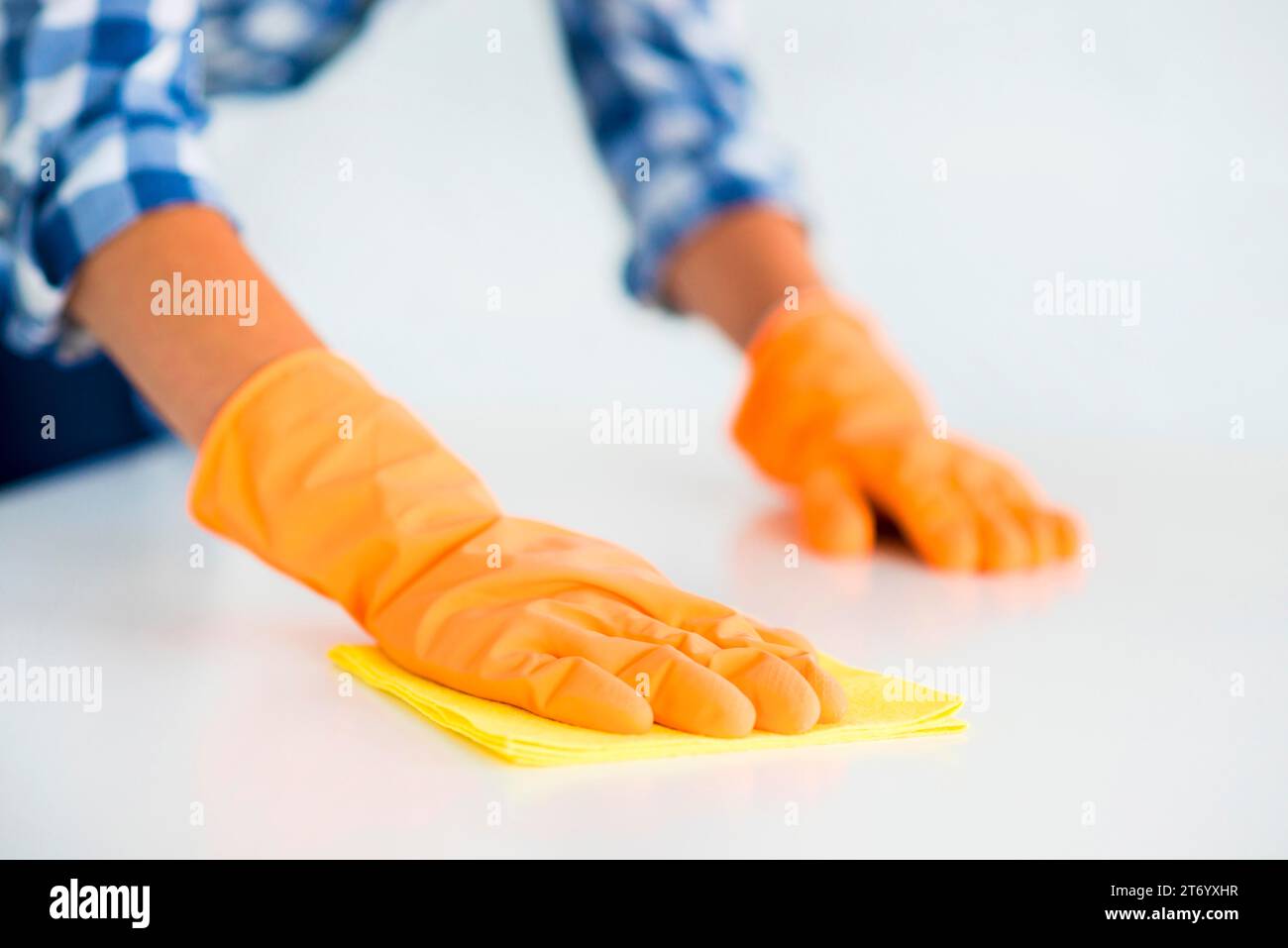 Woman s hand wearing orange gloves wipes white desk with yellow duster ...