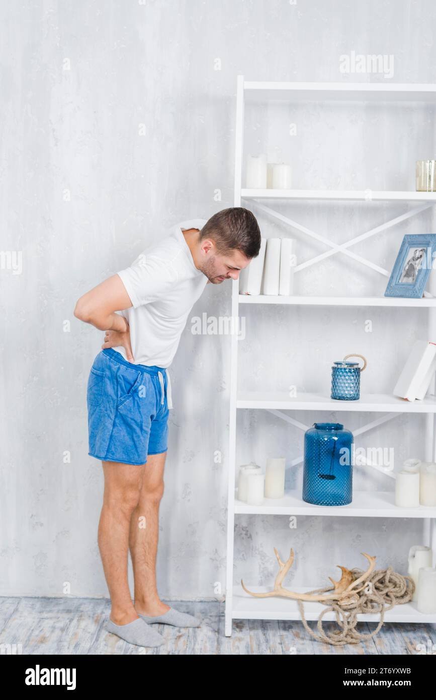 Young man standing near white shelf suffering from back pain Stock ...