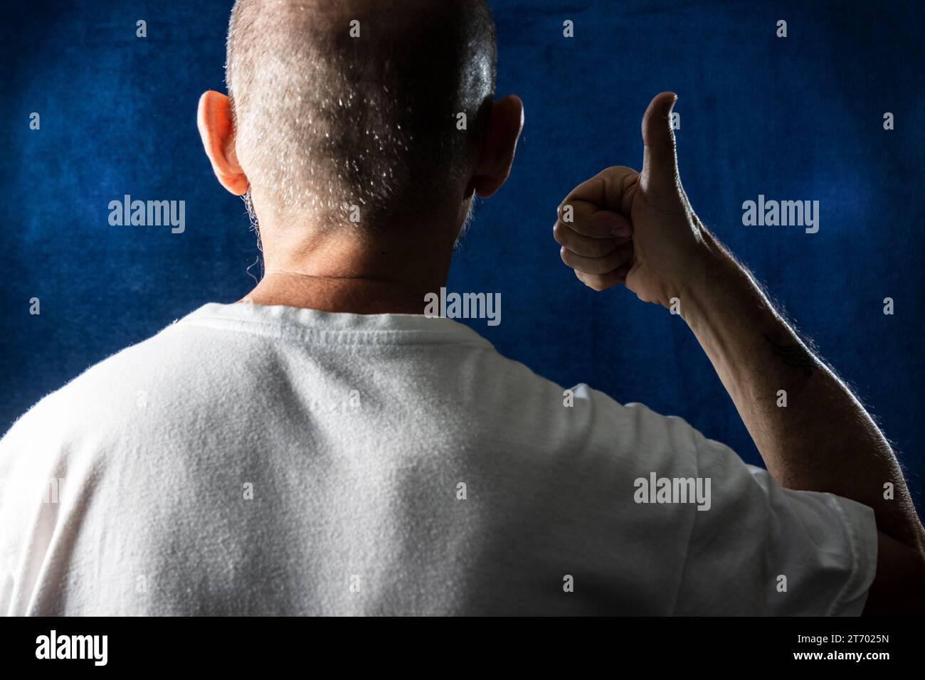 Man, with his back turned, making a sign with his hand against a blue ...