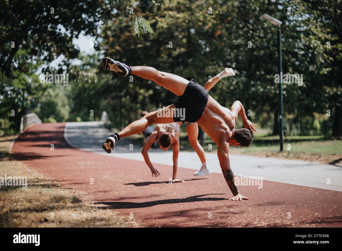 Fit sportspeople practice together in a sunny park doing cartwheels ...