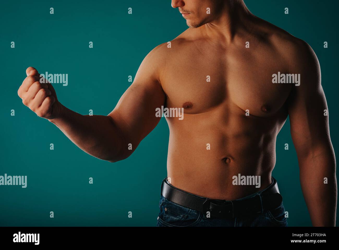 Young bodybuilder looking proudly at his biceps, posing on turquoise ...