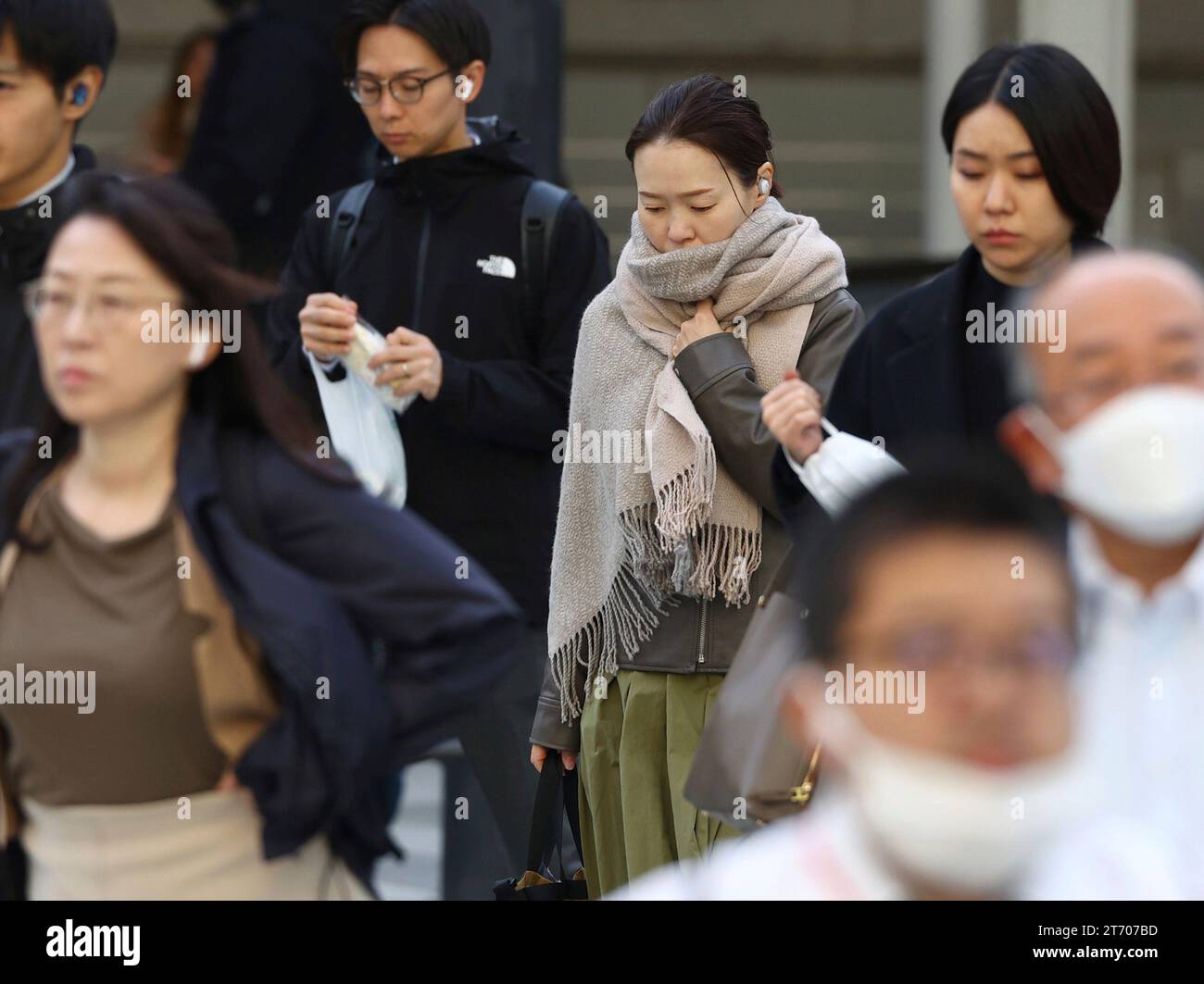 Commuters wearing thick clothes cross a street in front of Tokyo ...