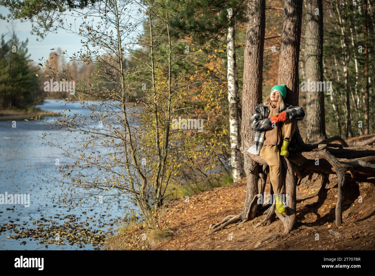Tranquil relaxed female sitting on large tree root with eyes closed ...
