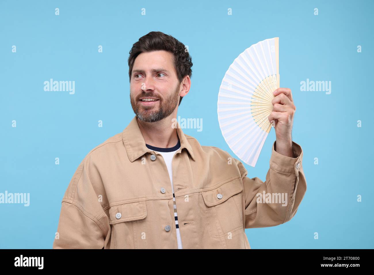 Happy man holding hand fan on light blue background Stock Photo - Alamy