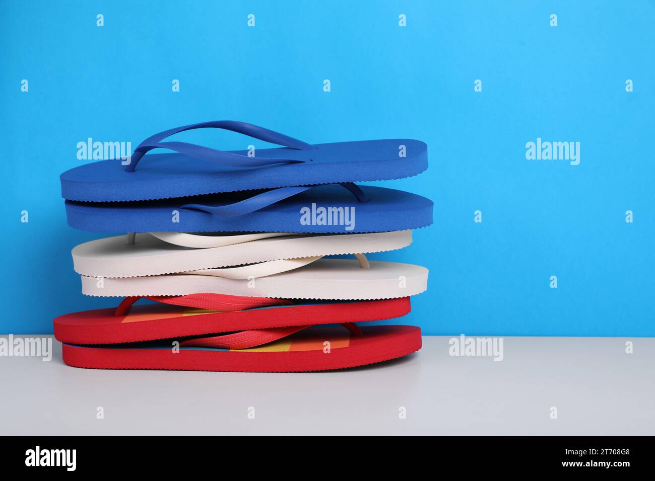 Stack of different flip flops on white table against light blue ...
