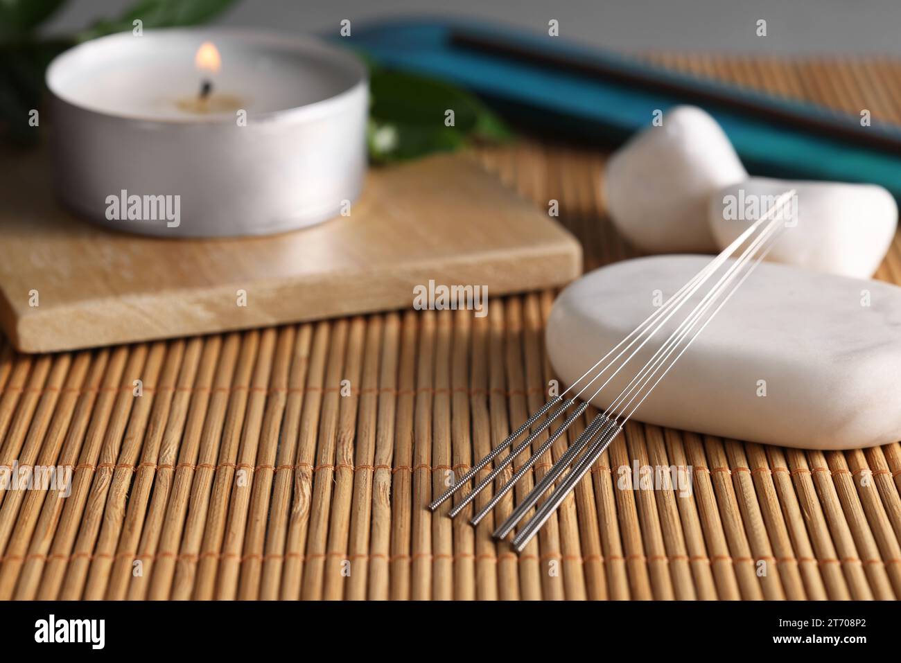 Acupuncture needles, spa stones and burning candle on bamboo mat. Space ...