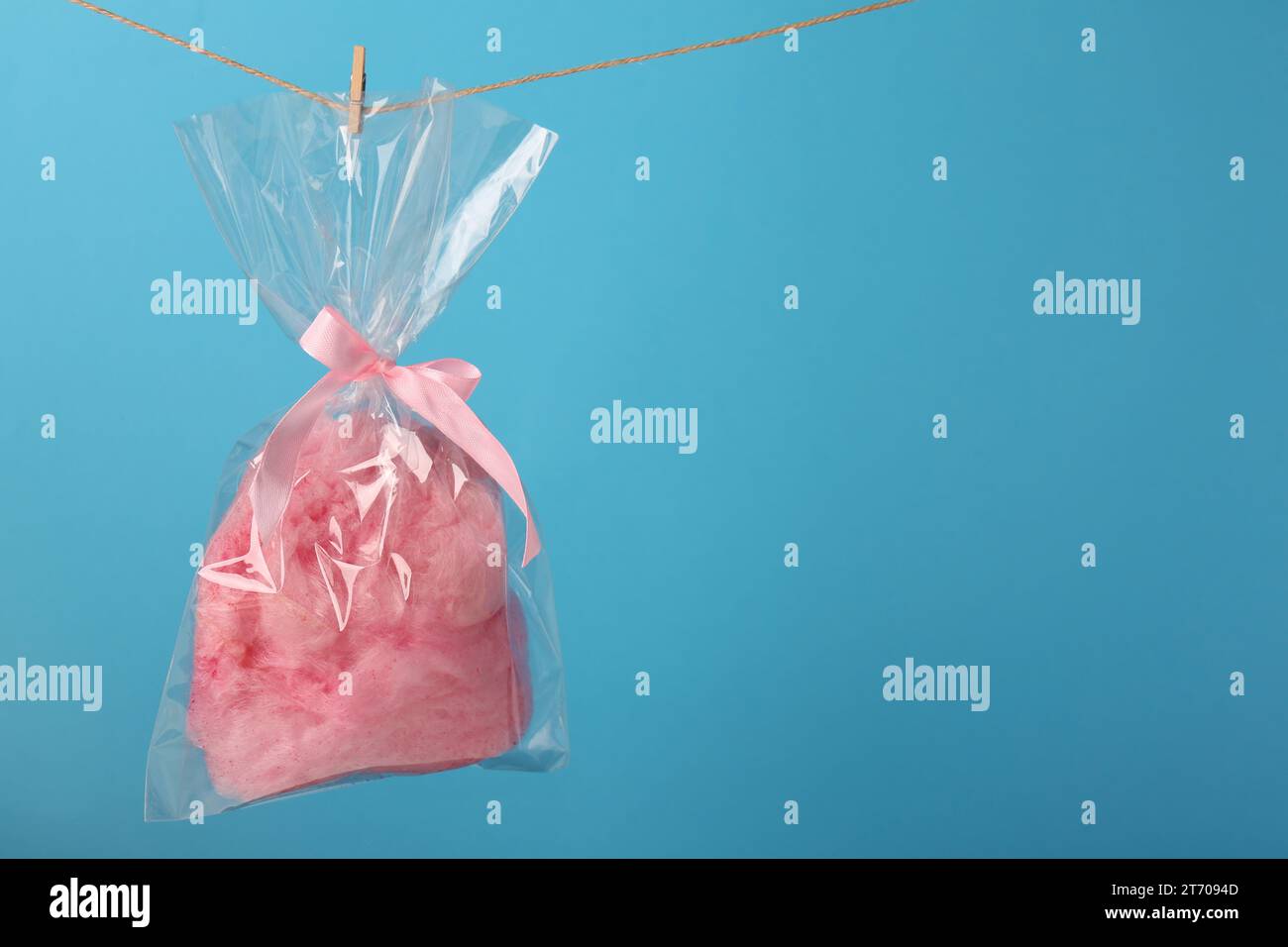 Packaged sweet pink cotton candy hanging on clothesline against light ...