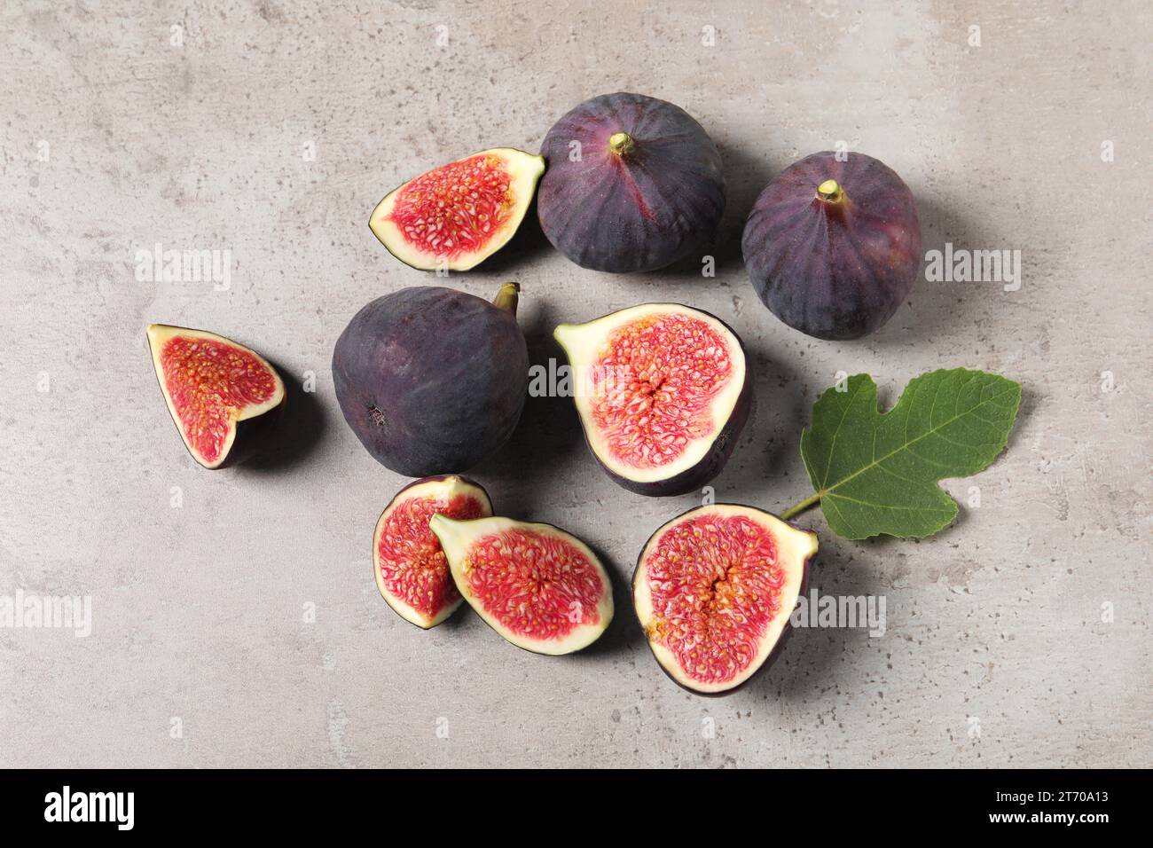 Whole and cut ripe figs with leaf on light grey textured table, flat ...