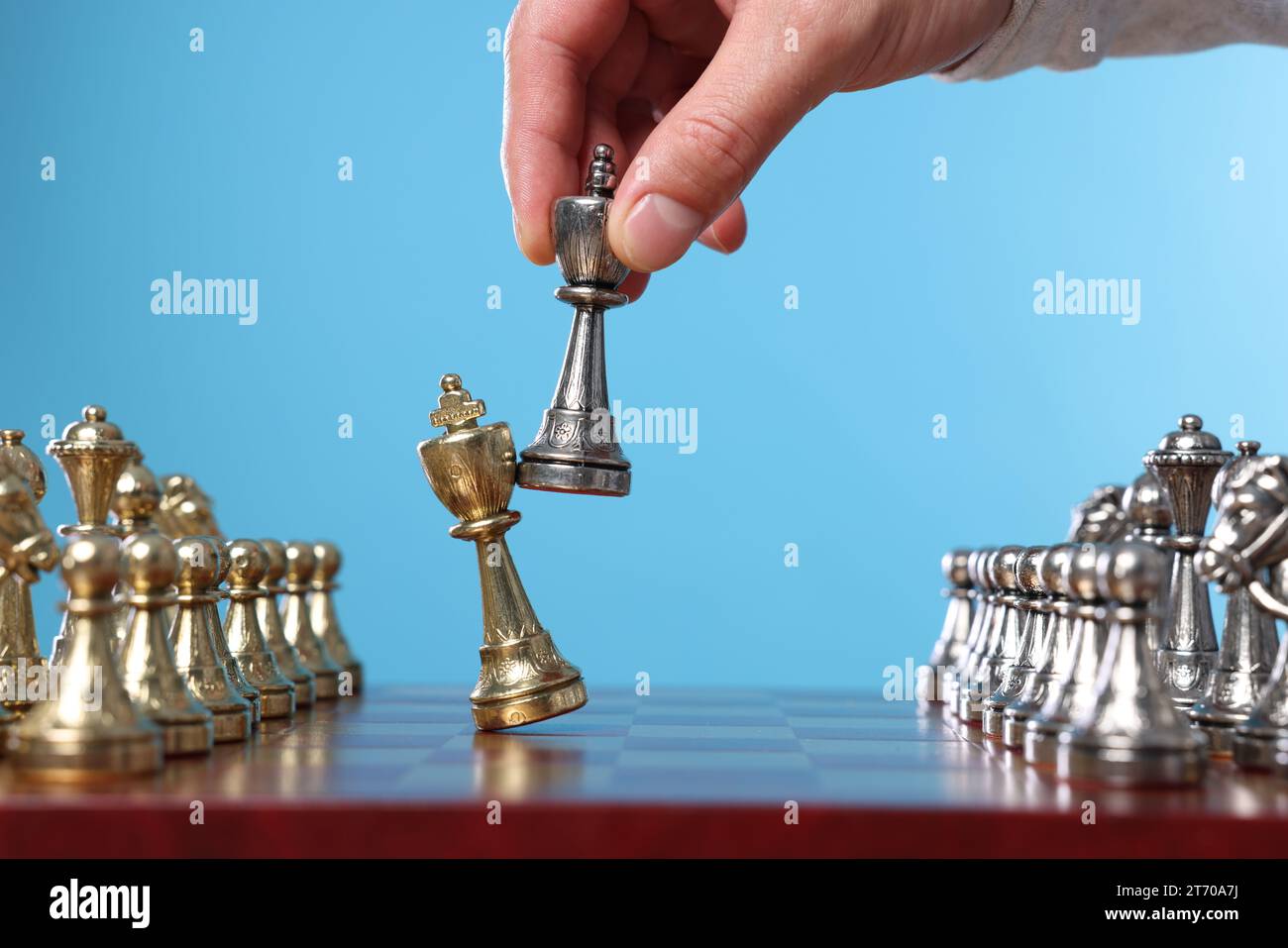 Man moving chess piece at checkerboard against light blue background ...