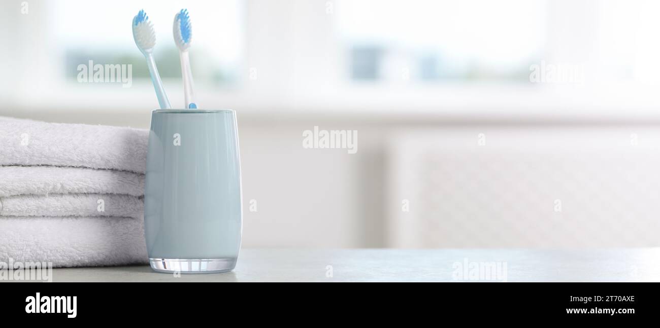 Plastic toothbrushes in holder and towels on white table indoors, space ...