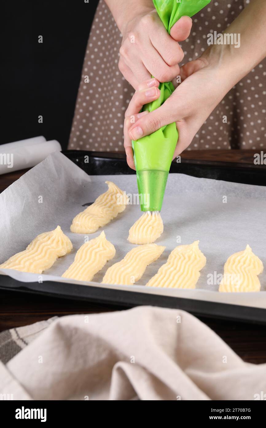 Making eclairs. Woman squeezing raw dough from pastry bag onto baking ...