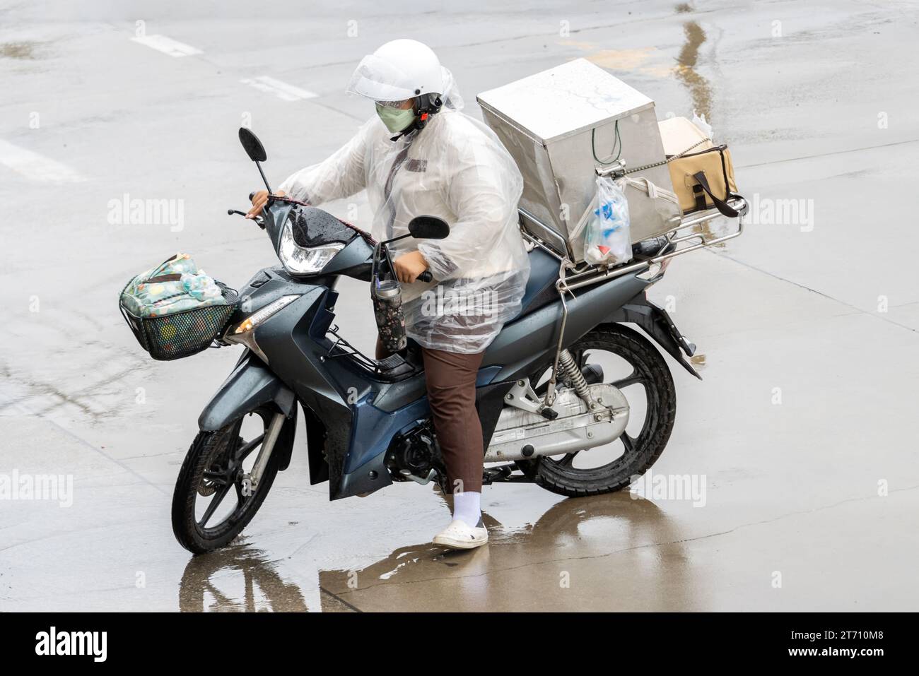 A delivery worker rides a motorcycle with a delivery box at rainy ...