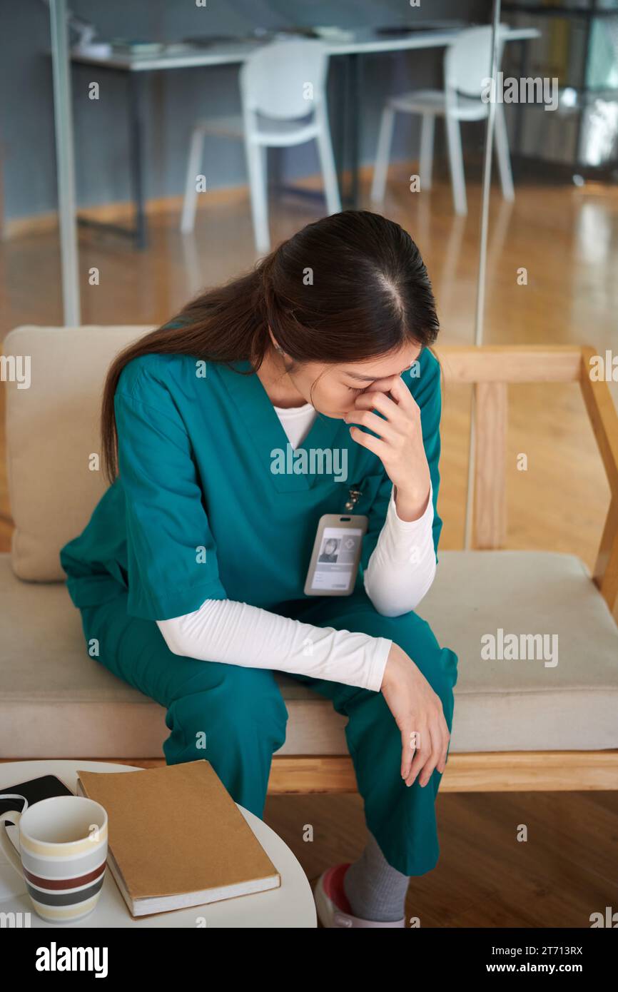 Stressed depressed medical nurse crying in hospital lounge area after ...