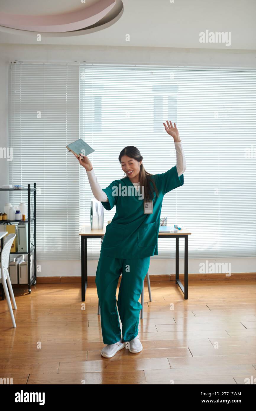 Medical nurse in green scrubs dancing in hospital lounge area after ...