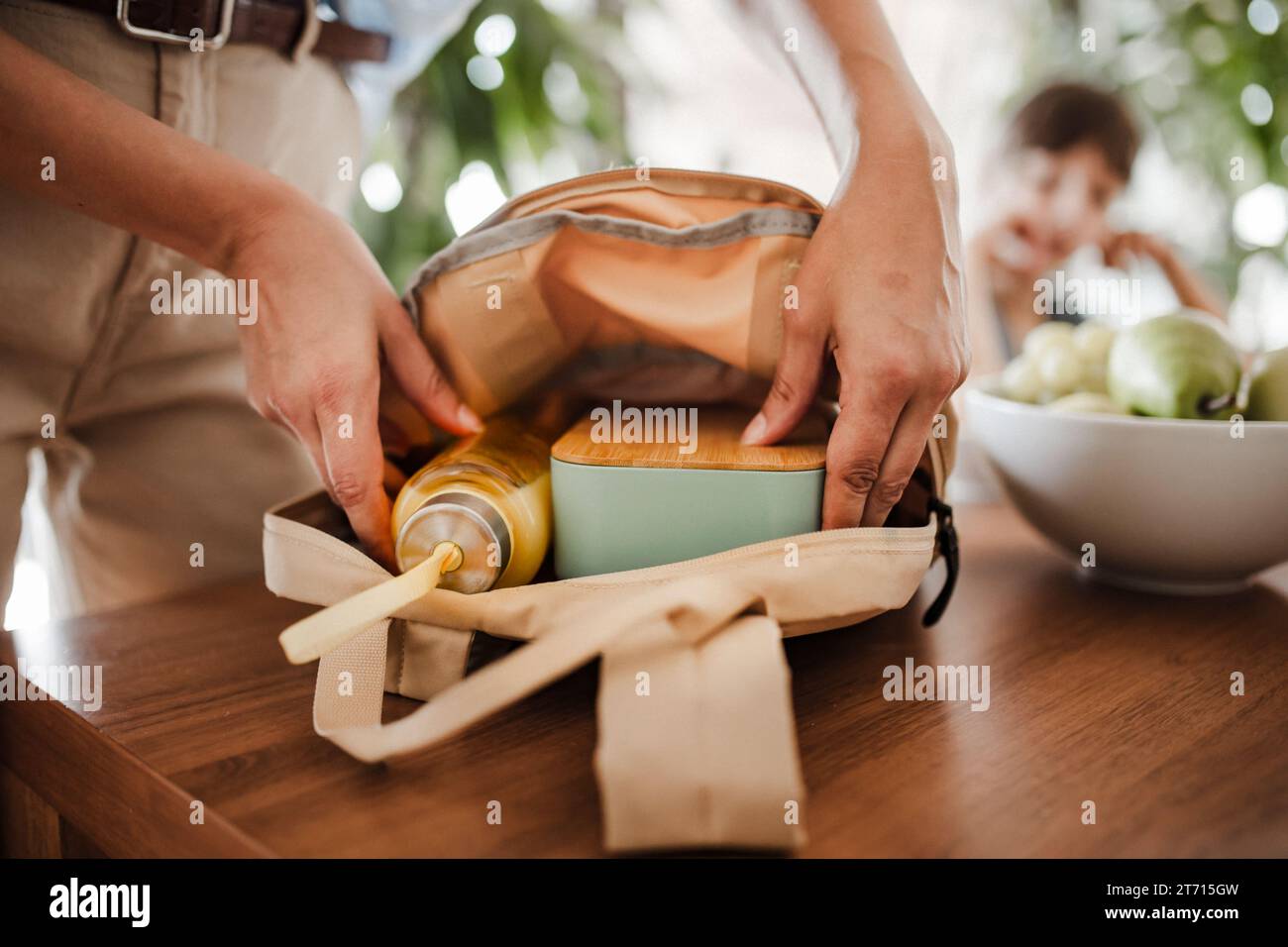 Mother packing school bag for kid. Putting bottle of juice, snacks for ...