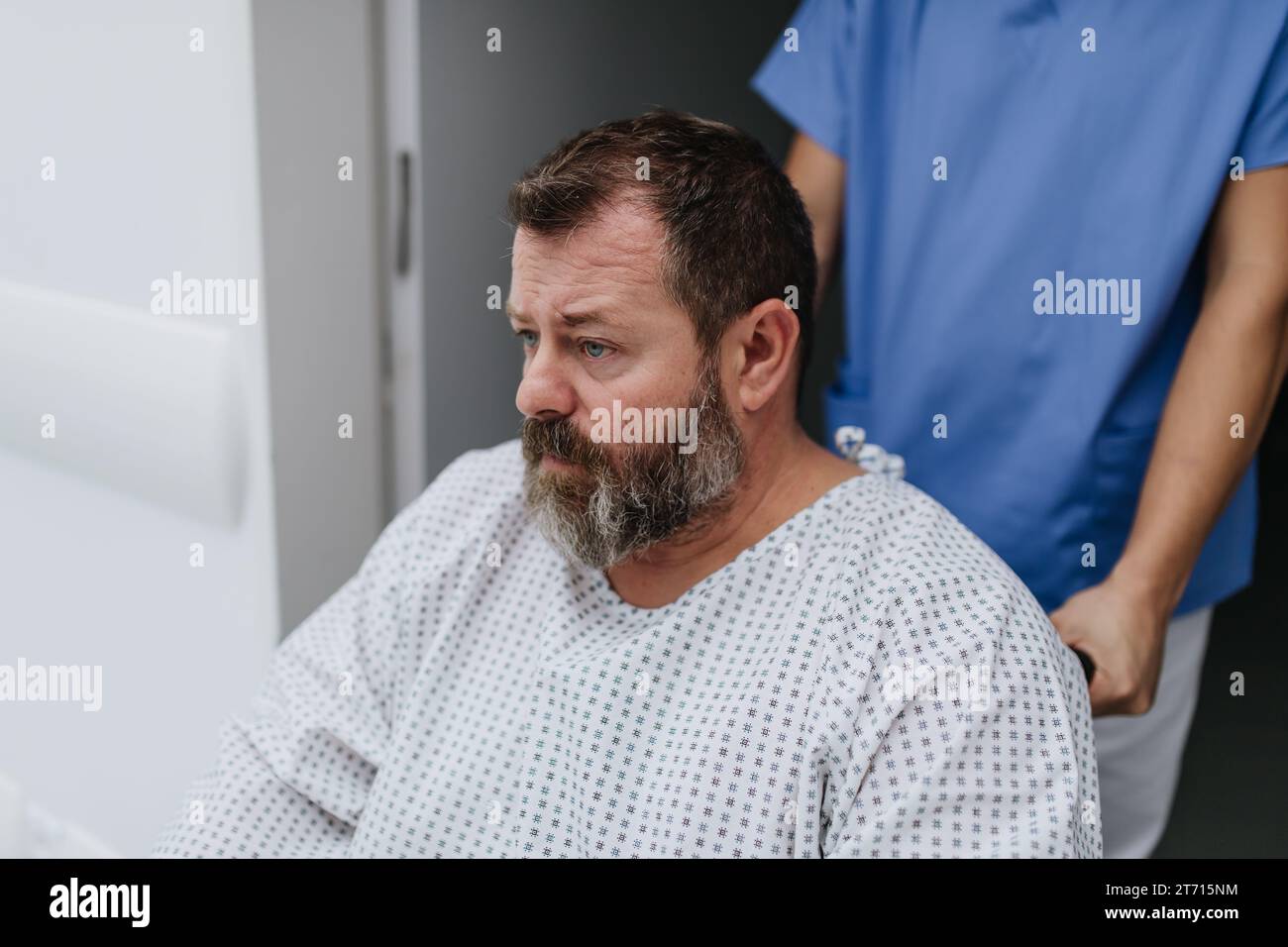 Male nurse pushing a patient in a wheelchair along a hospital corridor ...