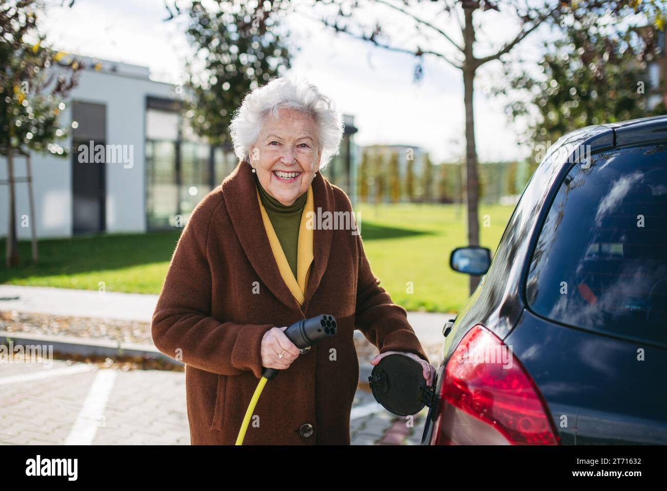 Close up of beautiful senior woman plugging charger in her electric car ...