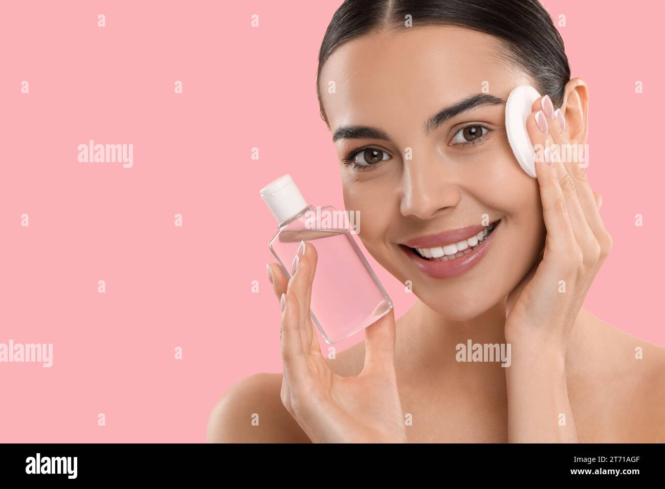 Beautiful woman removing makeup with cotton pad on pink background ...