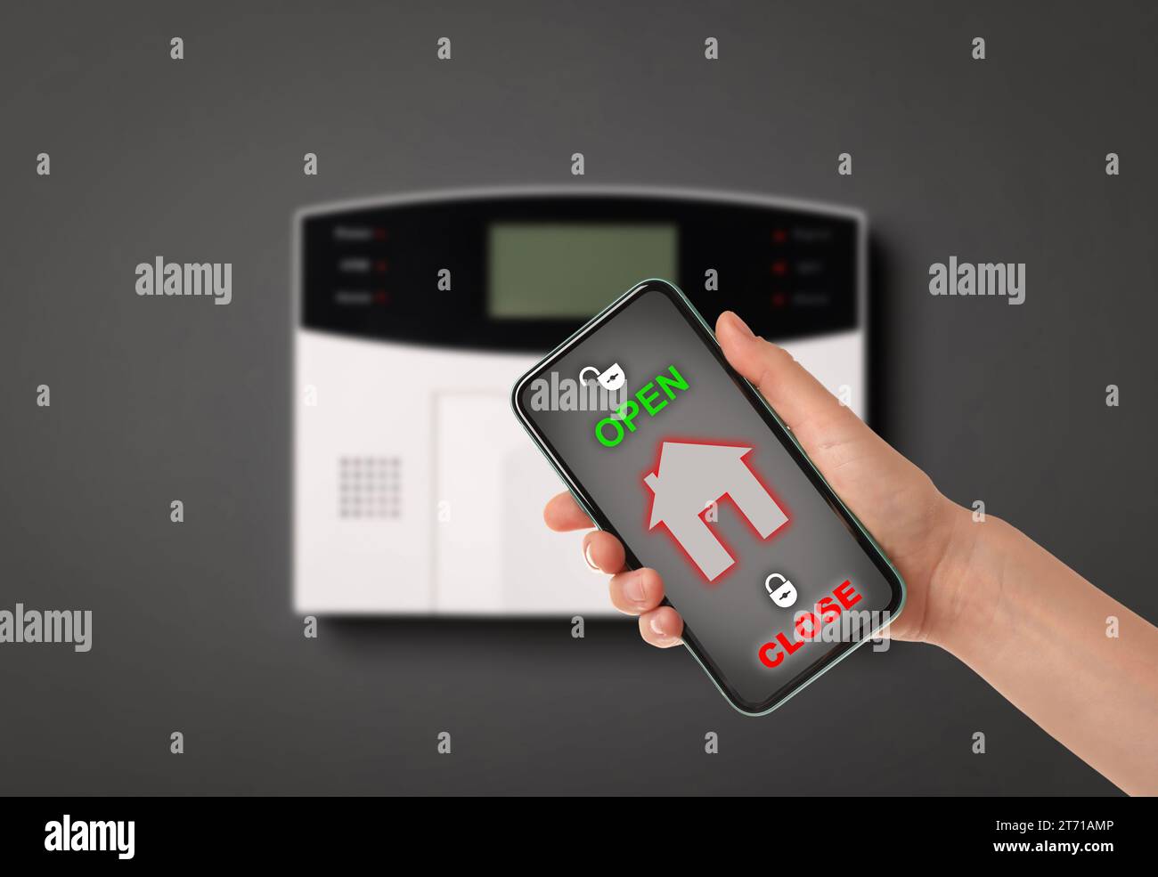 Woman operating home alarm system via mobile phone against dark wall ...