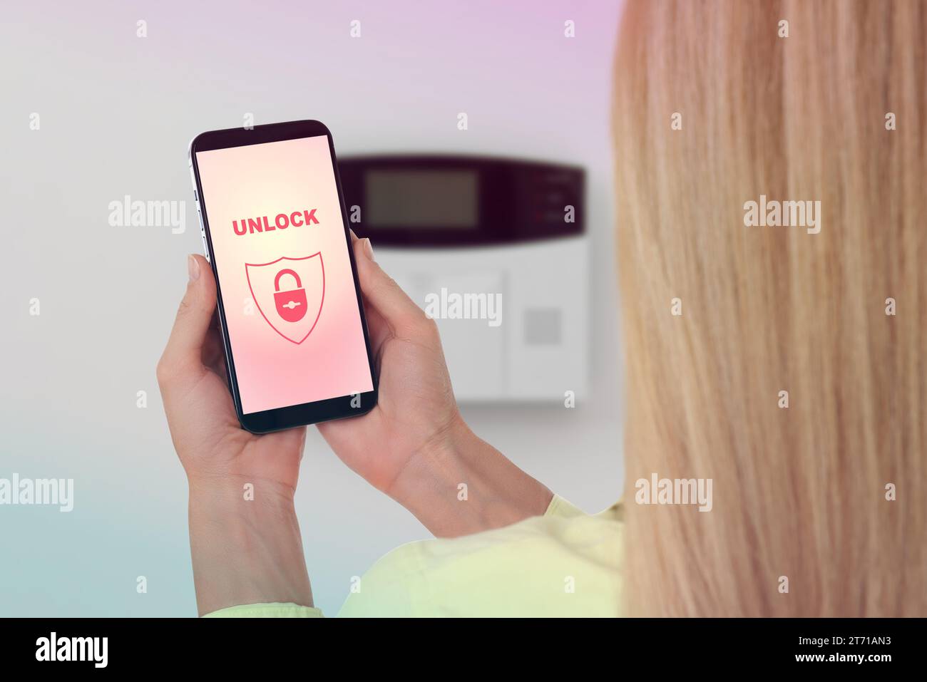 Woman operating home alarm system via mobile phone against white wall ...