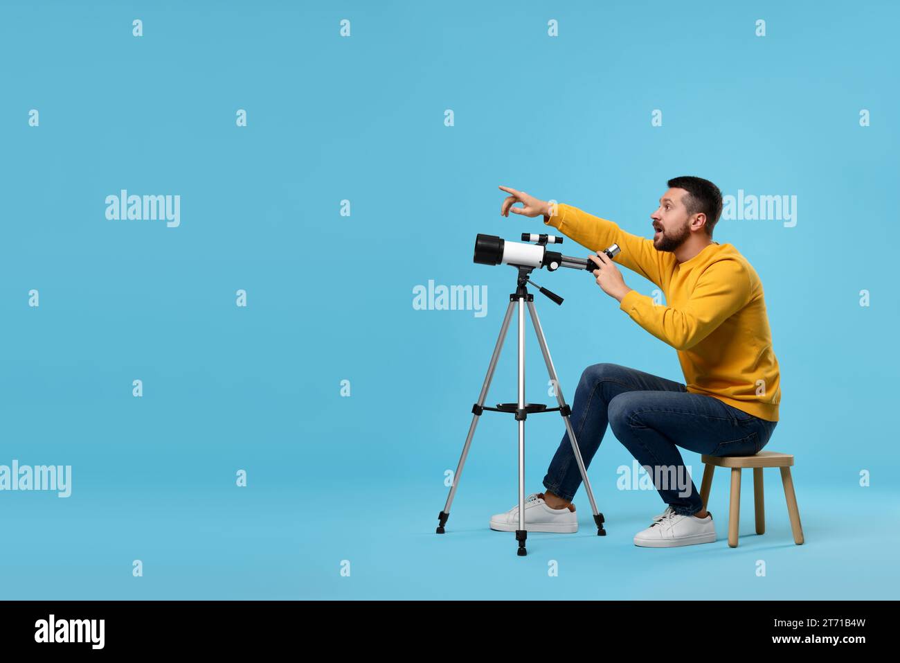 Excited astronomer with telescope pointing at something on light blue ...
