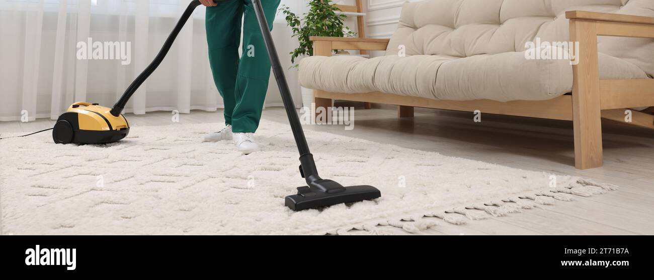 Dry cleaner's employee hoovering carpet with vacuum cleaner in room ...
